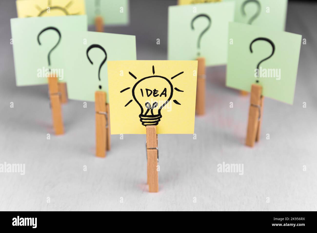 Light bulb doodle drawn on sticky note among many question marks. Hand ...