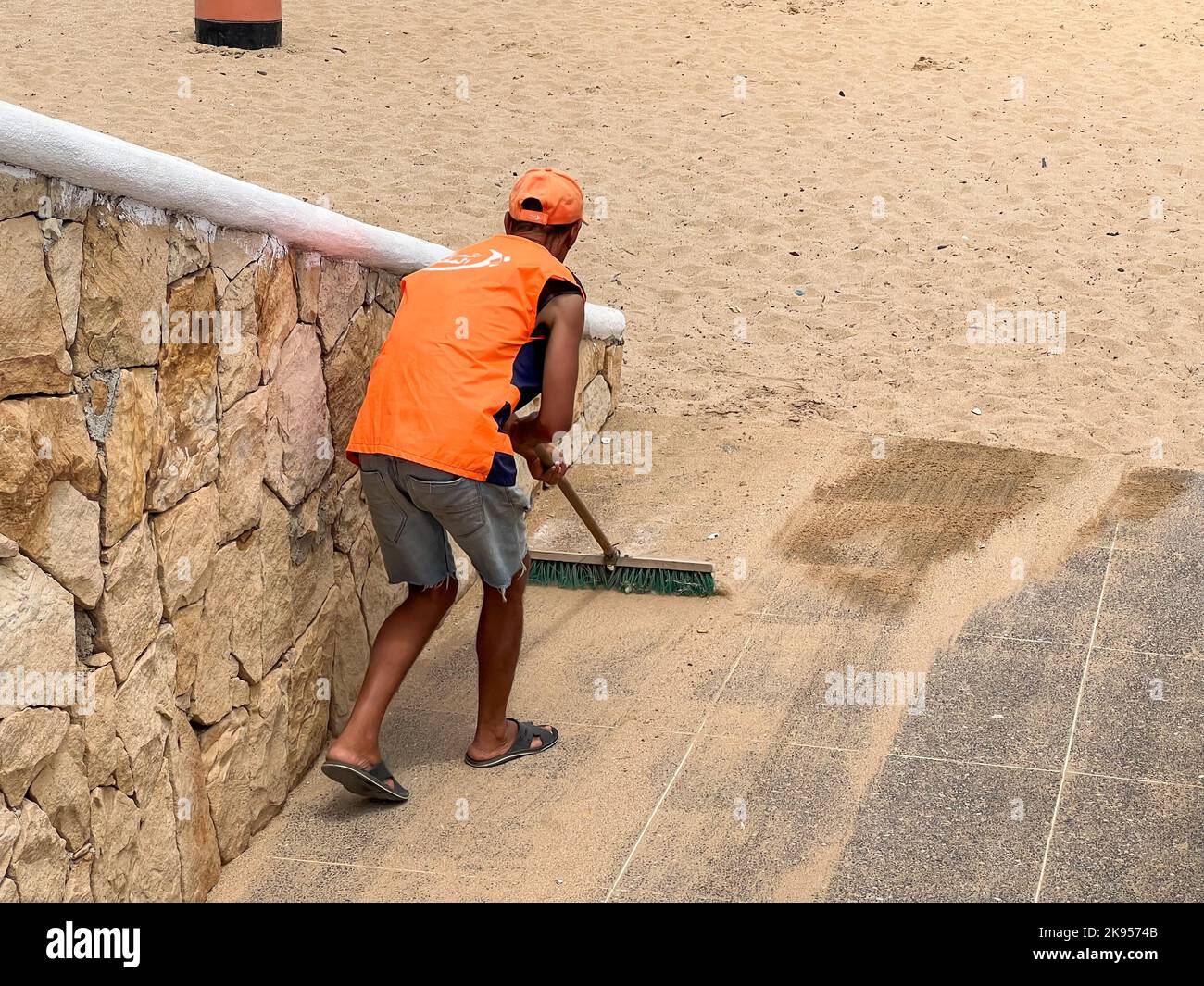 Cleaning man sweeping the pathway to the beach with a manual sweeper ...