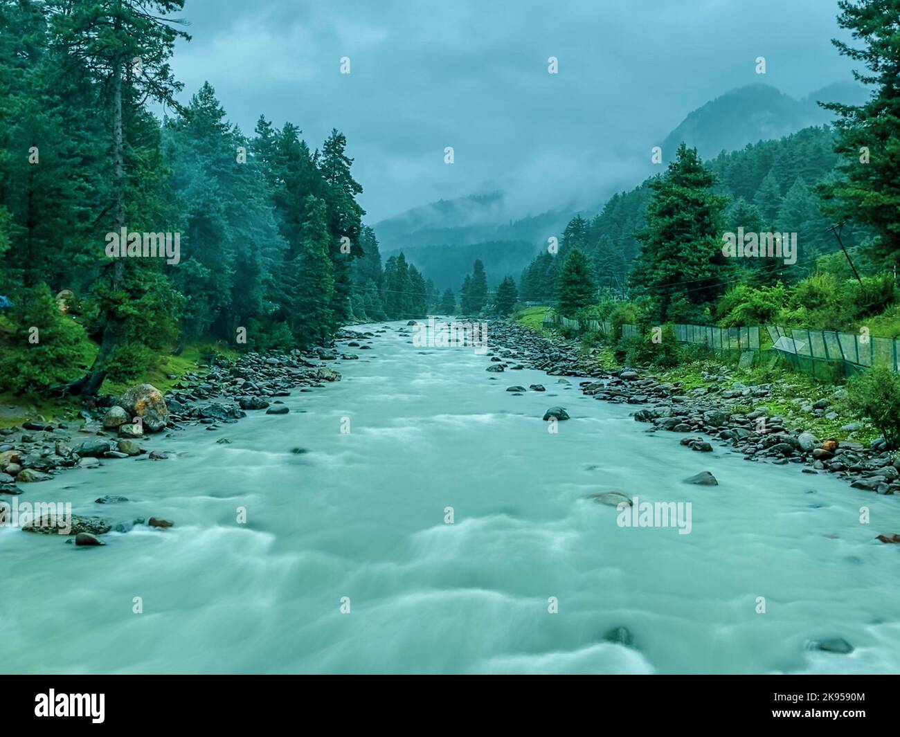 A rocky river in the middle of the forest with mountains in the ...