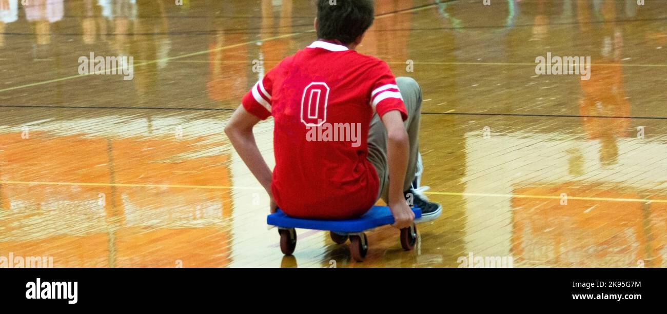 Boy sitting on a scotter moving backwards on a gym floor Stock Photo ...