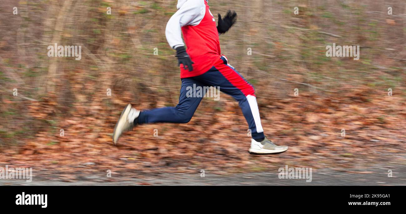 Side view of a high school runner running fast in the woods with the ...