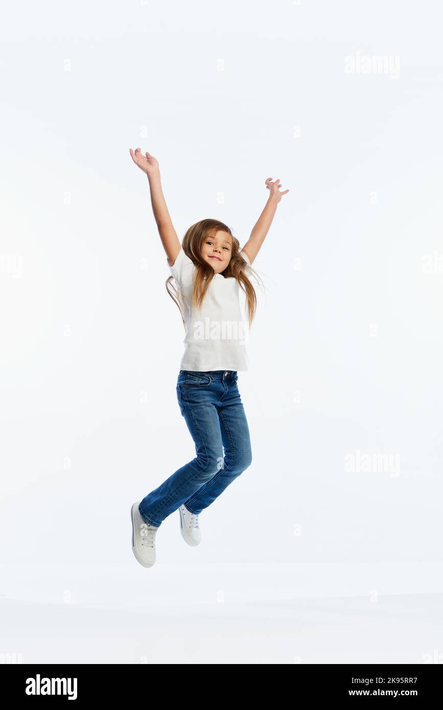 Happy little girl, pupil in casual style clothes jumping with rejoice ...
