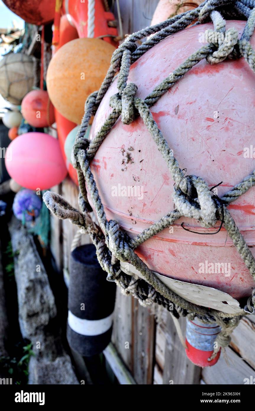 Colourful old fishing floats and buoys strung along a boatyard wall ...