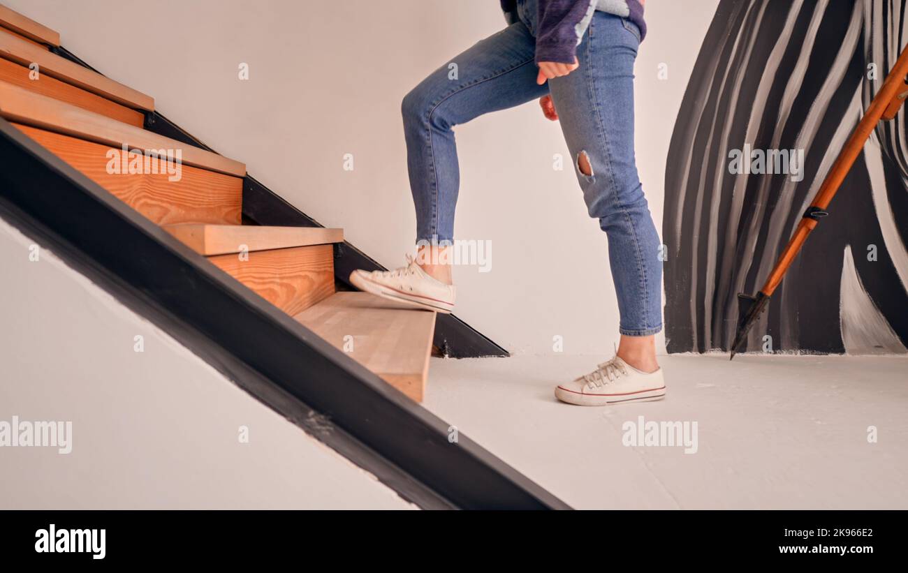 The legs of a young female in jeans and sneakers going up wooden stairs ...