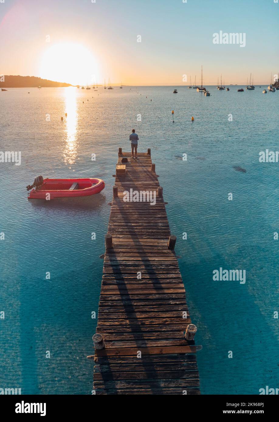 A beautiful shot of a wooden pier and a red boat at Santa Guilia beach ...