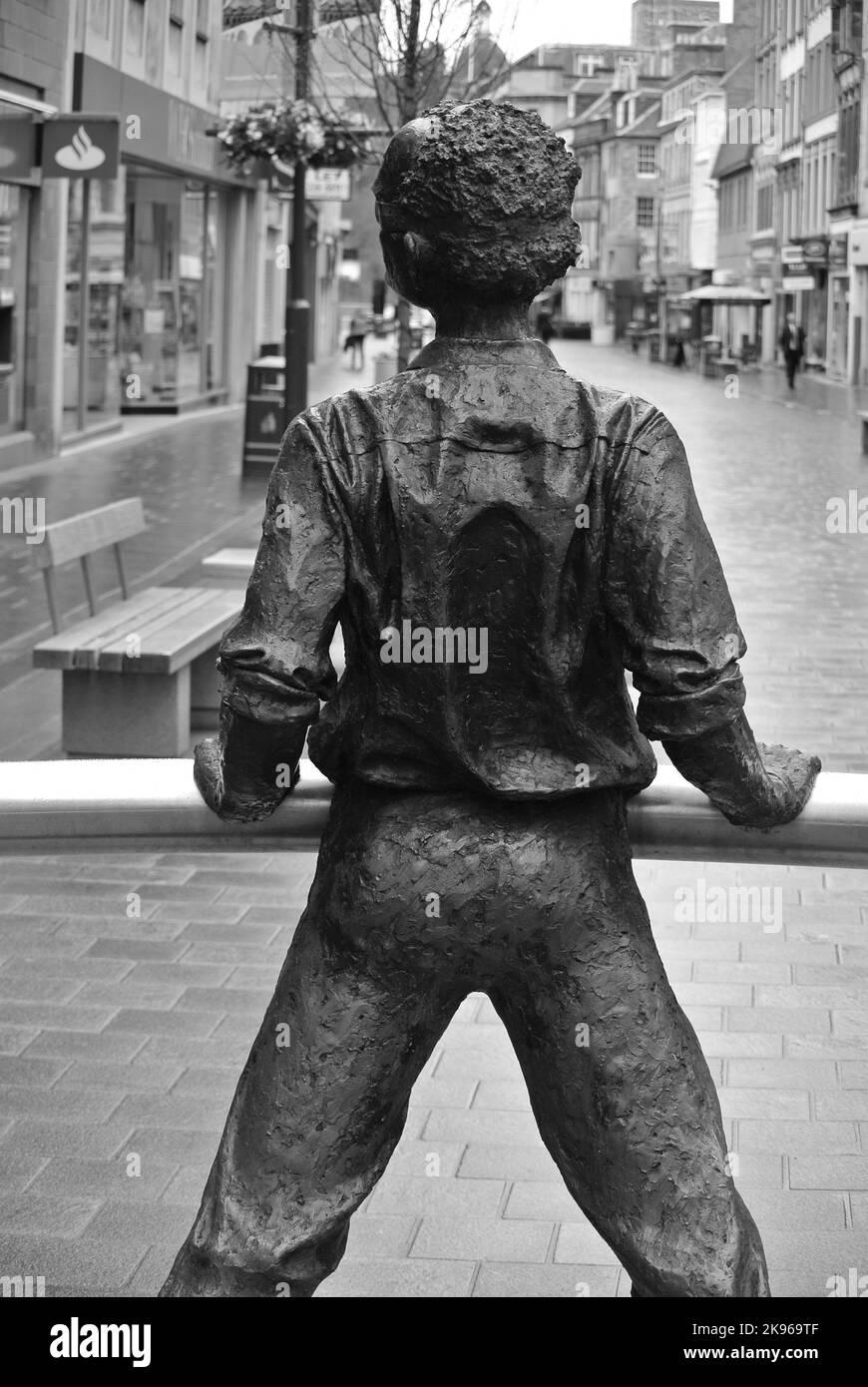A vertical grayscale of a rear view of a statue looking down at a ...
