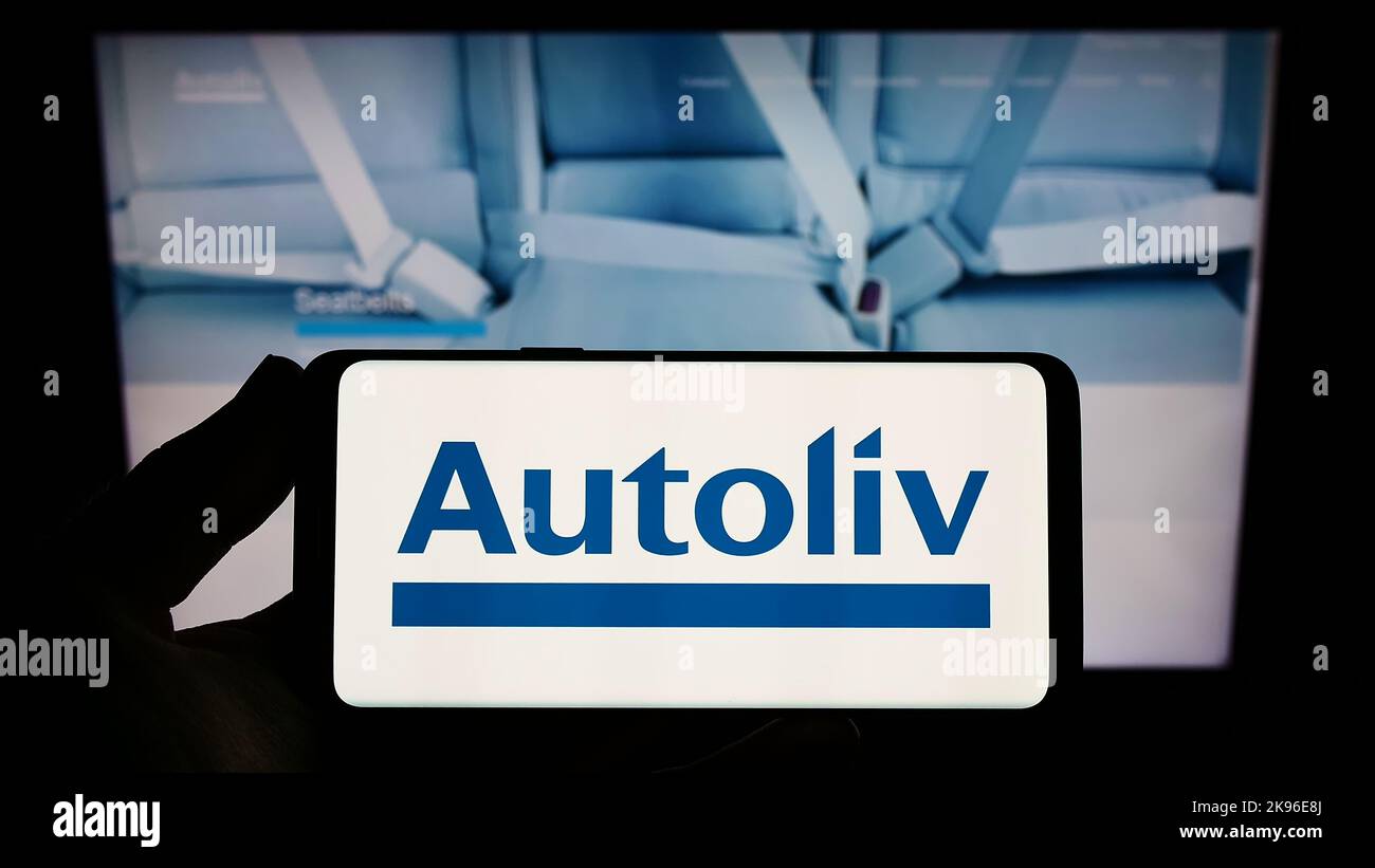 Person holding smartphone with logo of automotive supply company Autoliv Inc. on screen in front ...