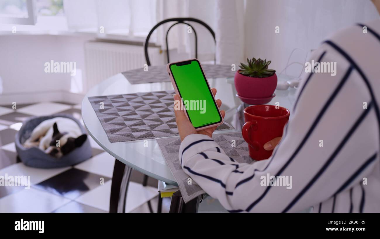 A woman using their phone with a green screen effect while drinking tea ...