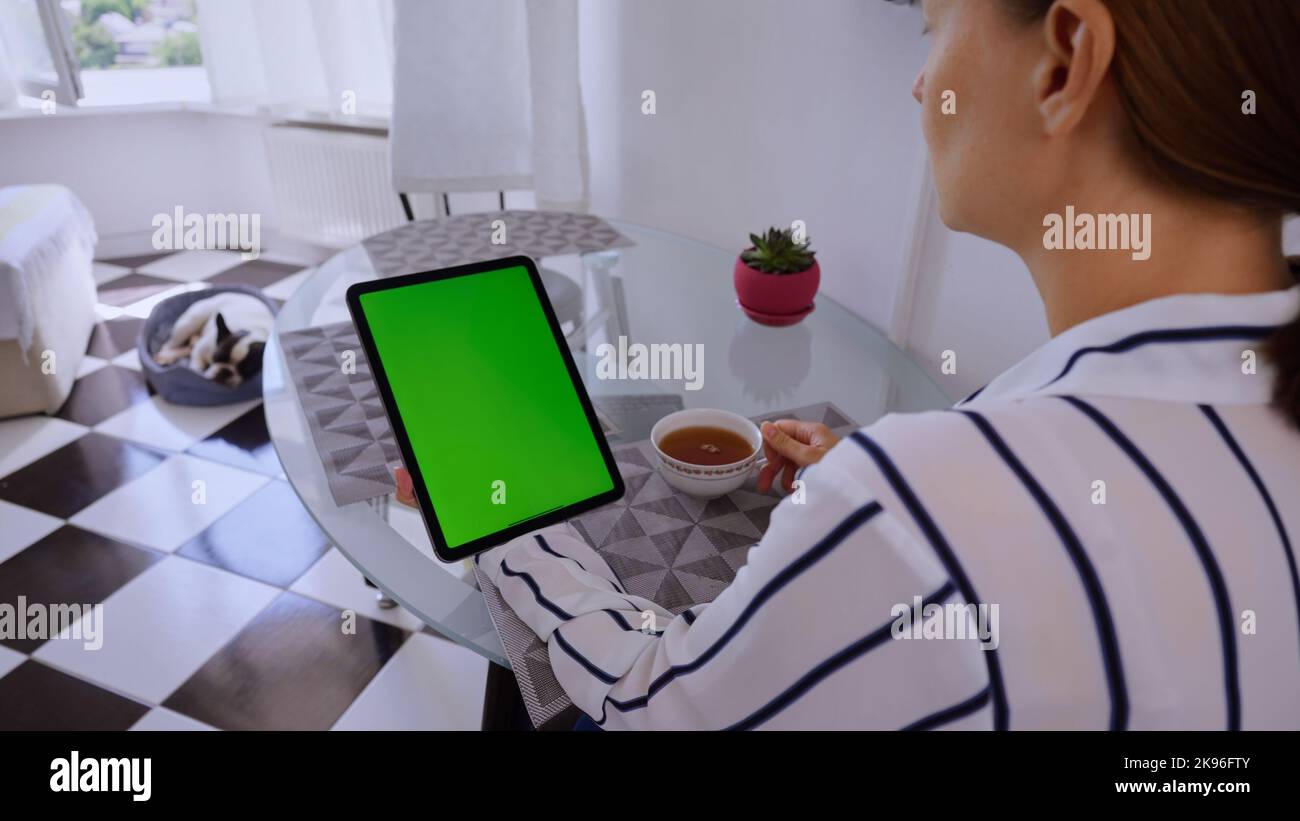A woman using a tablet with a green screen effect while drinking tea ...