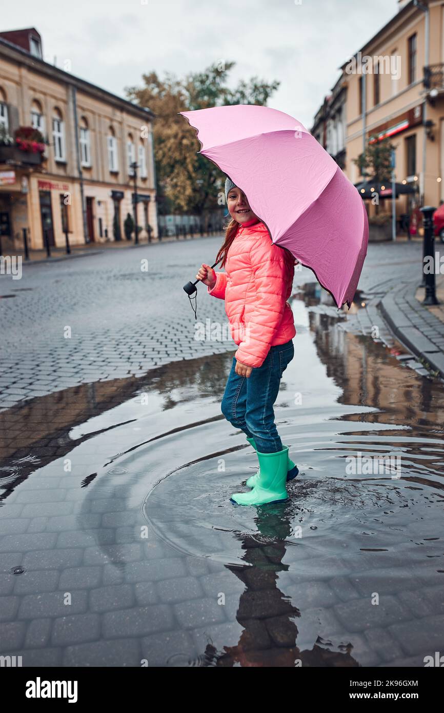 Child holding big pink umbrella walking through the puddle in a ...