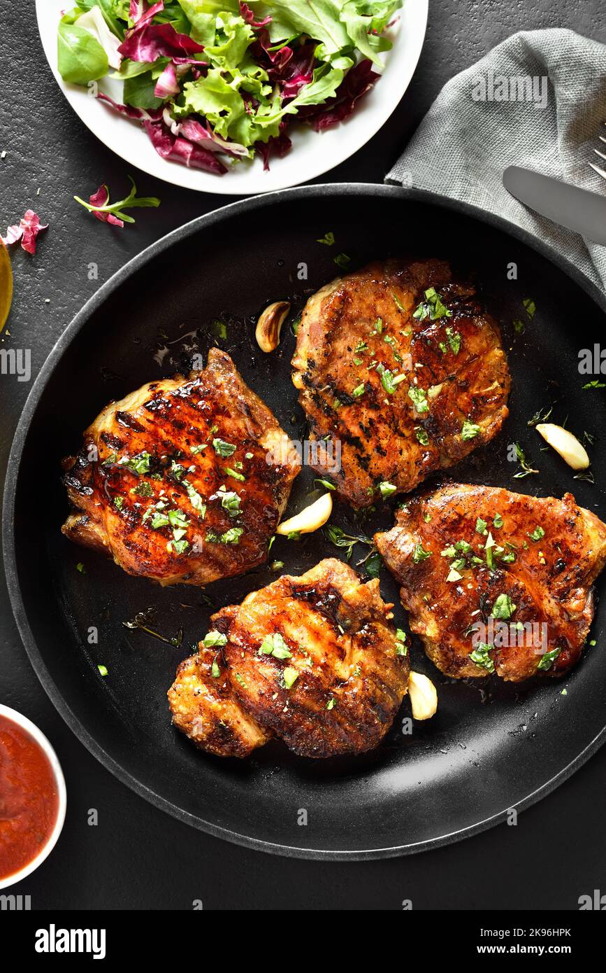 Roasted pork steaks in frying pan over black stone background. Top view, flat lay, close up ...