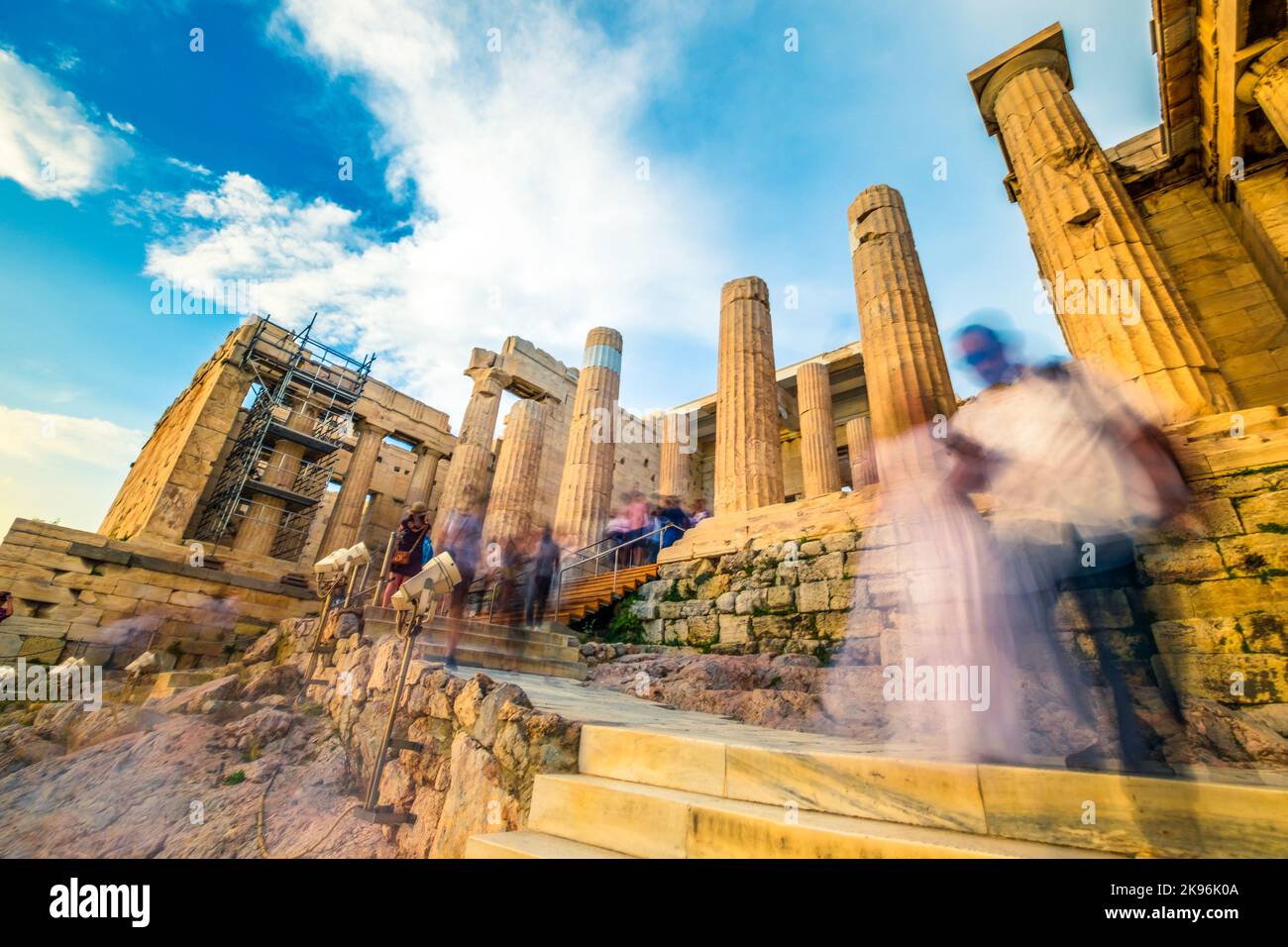Crowd of tourists walking around in front of the ancient ruins of Parthenon building at sunset ...