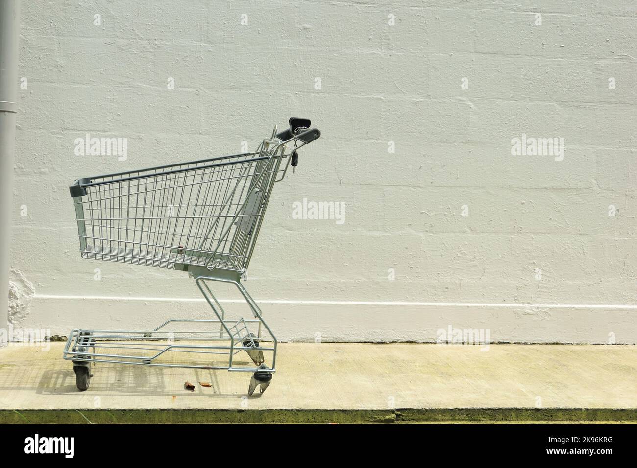 empty shopping trolley left outside against white wall Stock Photo - Alamy
