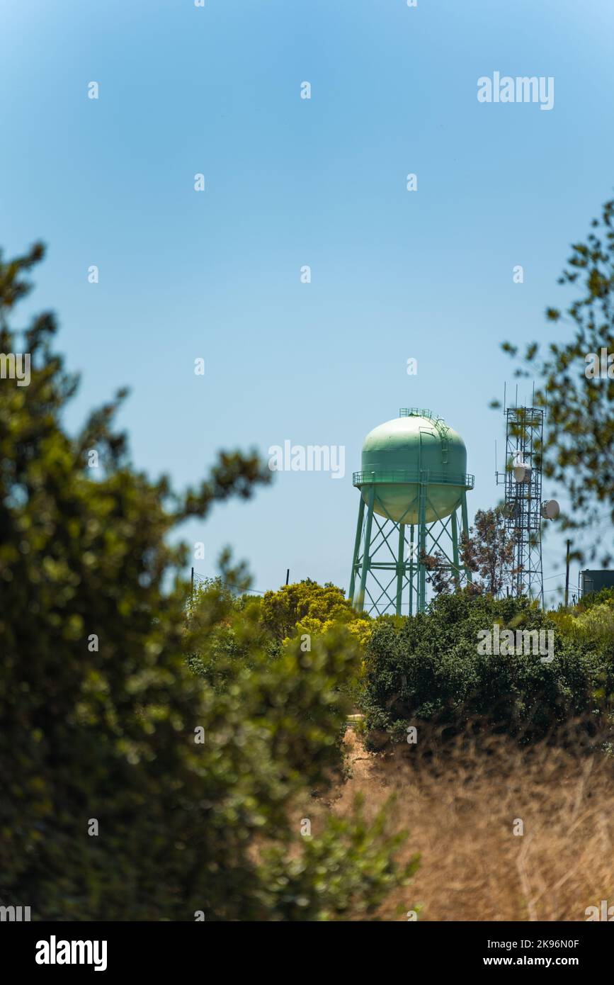 A vertical shot of a water tank seen through bushes and trees with ...