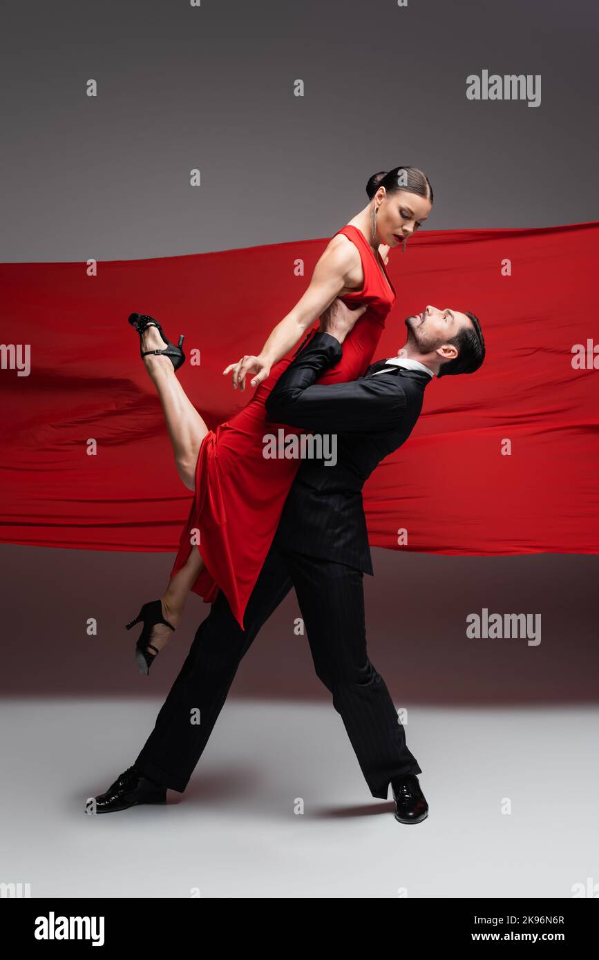 Dancer in suit lifting elegant partner while performing tango on grey ...