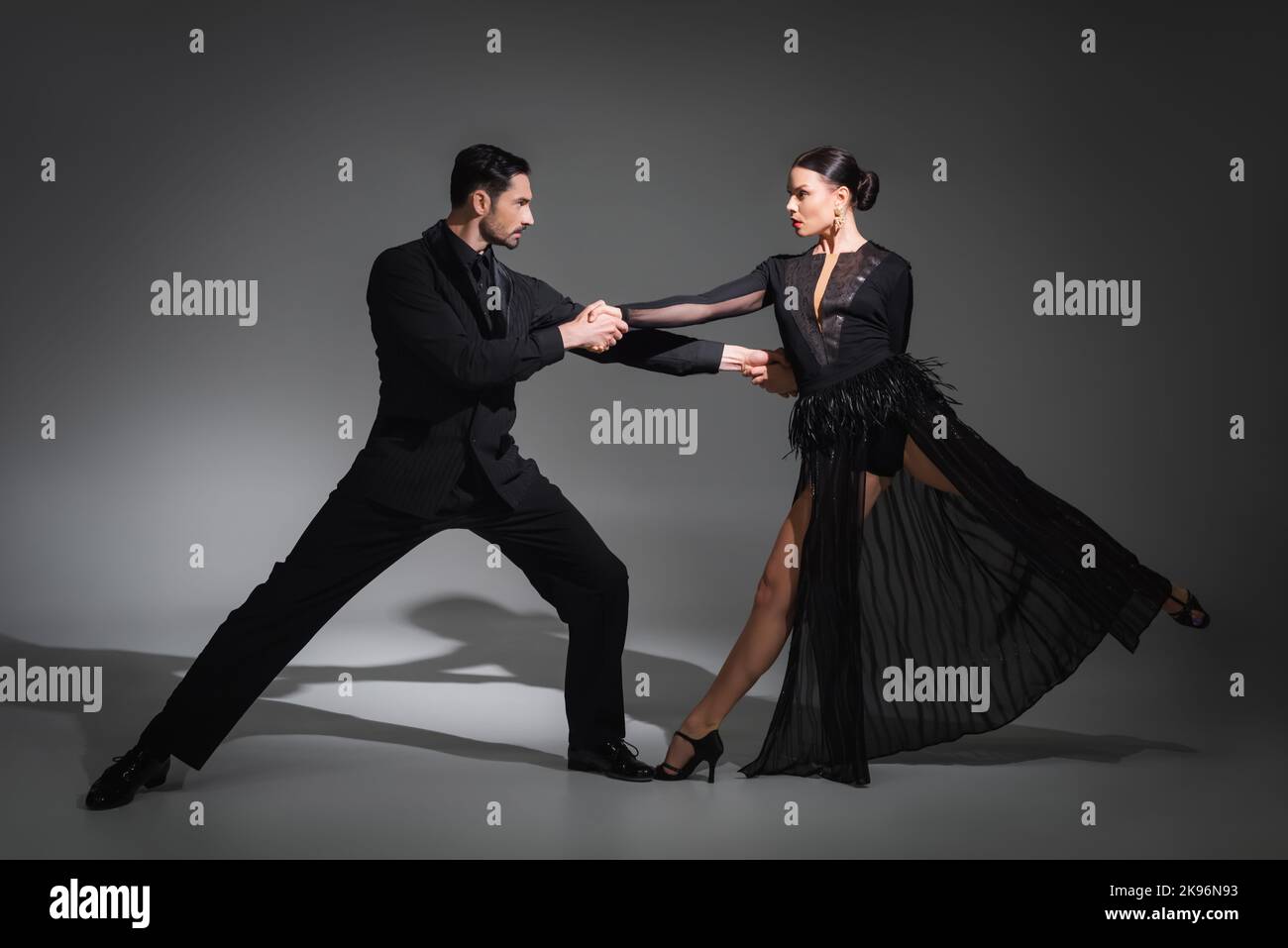 Side view of elegant couple performing tango on grey background with ...
