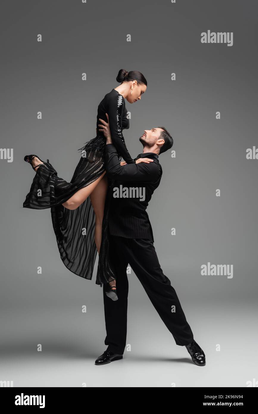 Side view of professional ballroom dancer lifting partner on grey ...