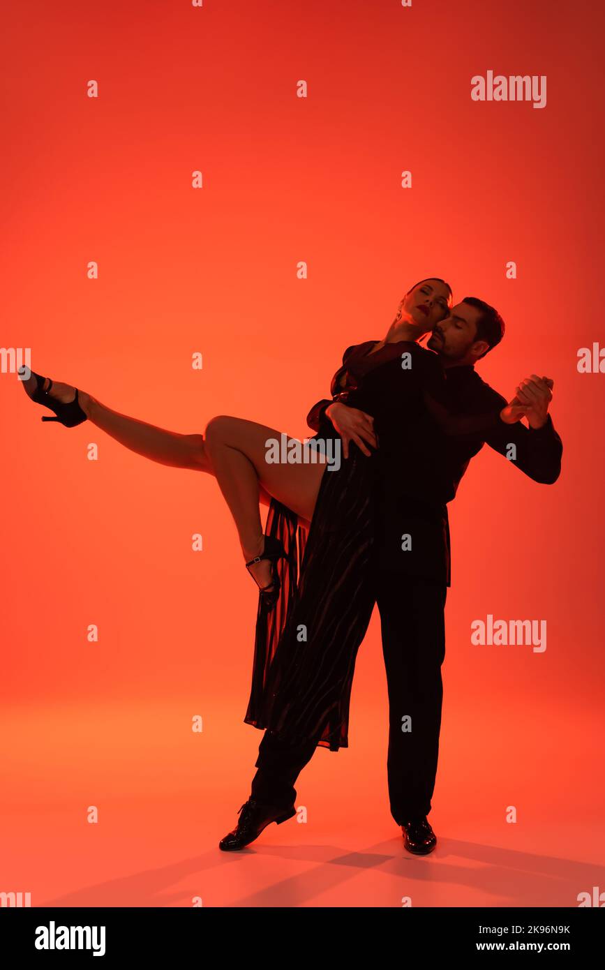 Elegant woman holding hands while dancing tango on red background with ...