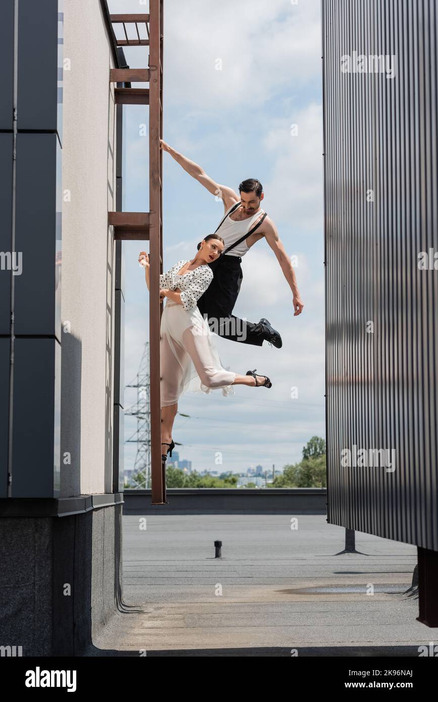 Professional dancers posing on ladder on rooftop of building at daytime ...