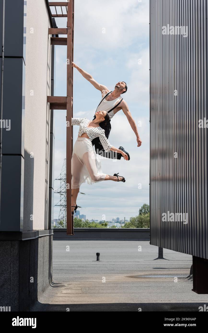 Positive dancers posing on ladder on rooftop of building at daytime ...