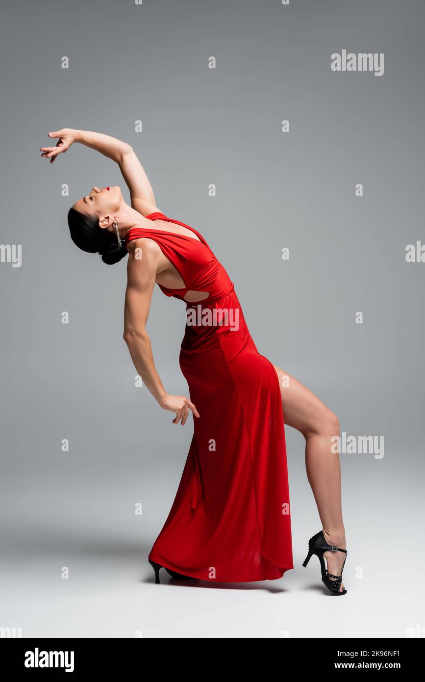 Side view of professional ballroom dancer in red dress moving on grey ...