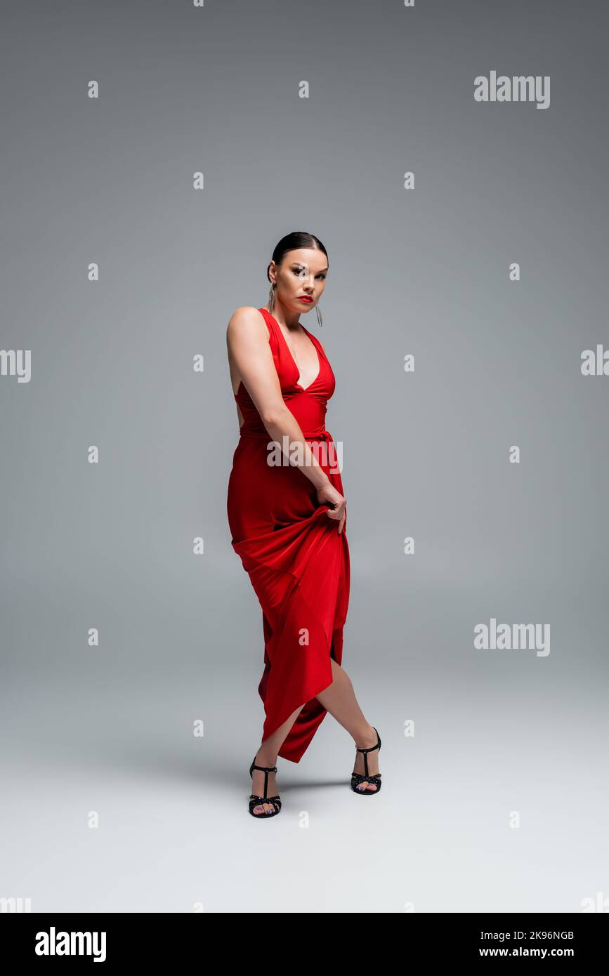 Stylish ballroom dancer in red dress and heels looking at camera on ...