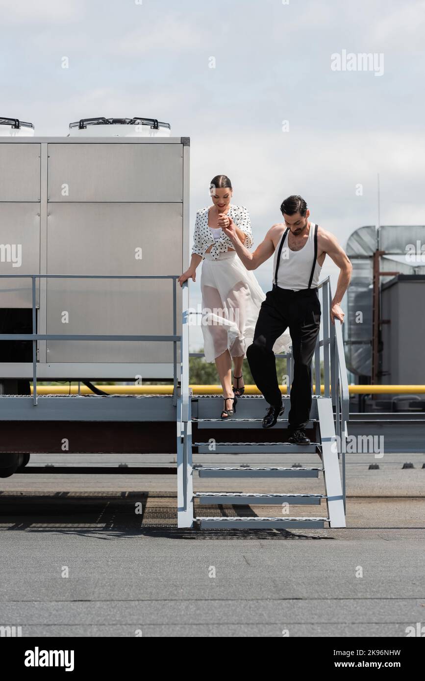 Stylish pair of dancers holding hands while walking on stairs on roof ...