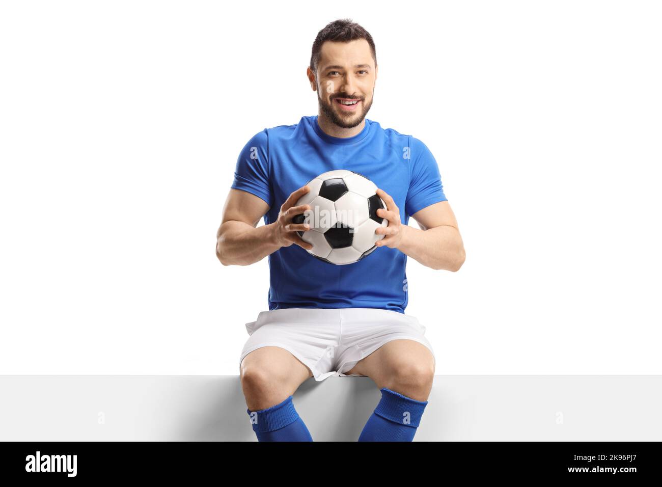 Football player sitting on a blank panel and holding a soccer ball ...