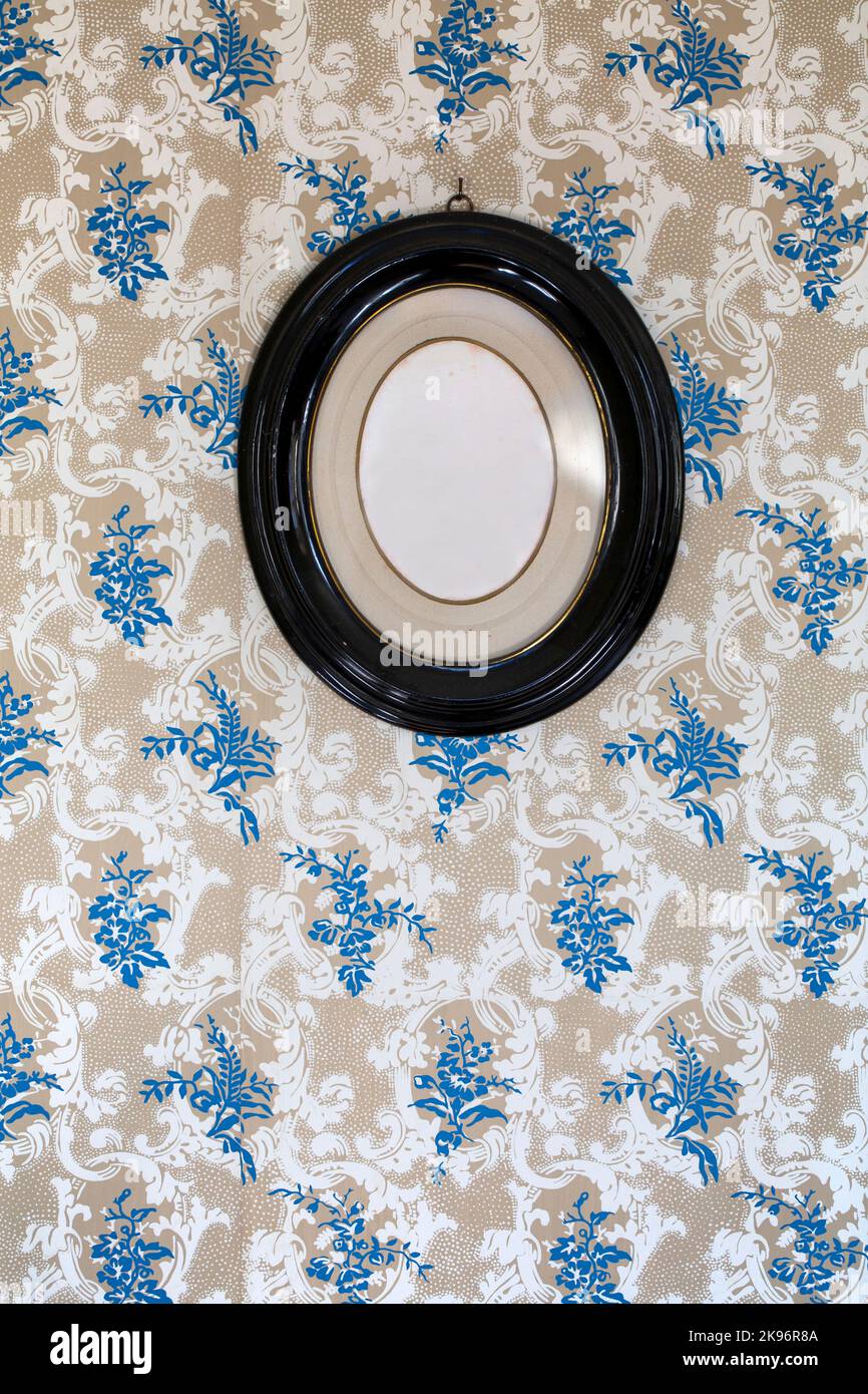 Vintage blank oval picture frame hanging on a wallpaper decorated wall ...
