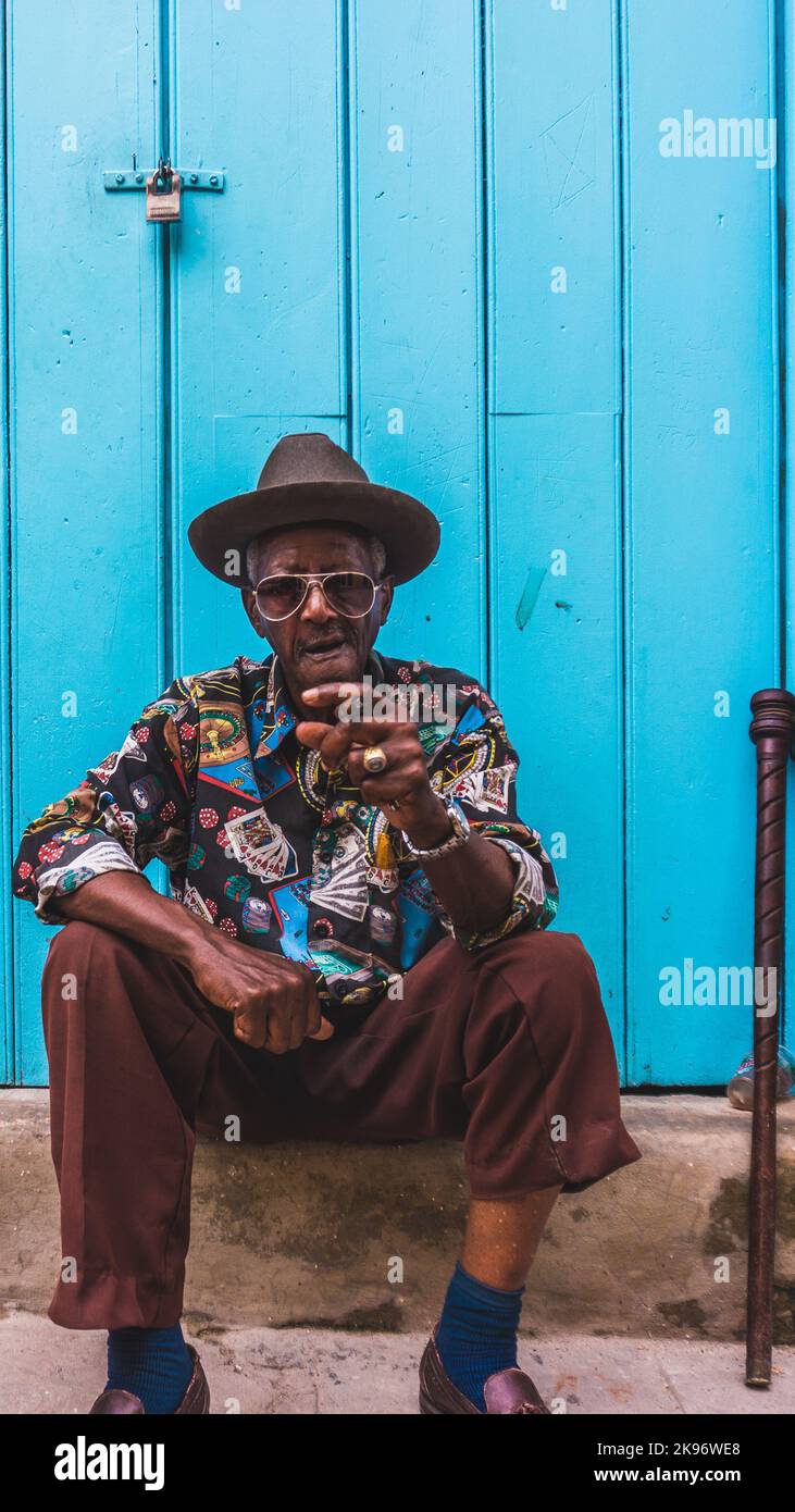 A black, Cuban man smoking his cigar while sitting in front of a blue ...