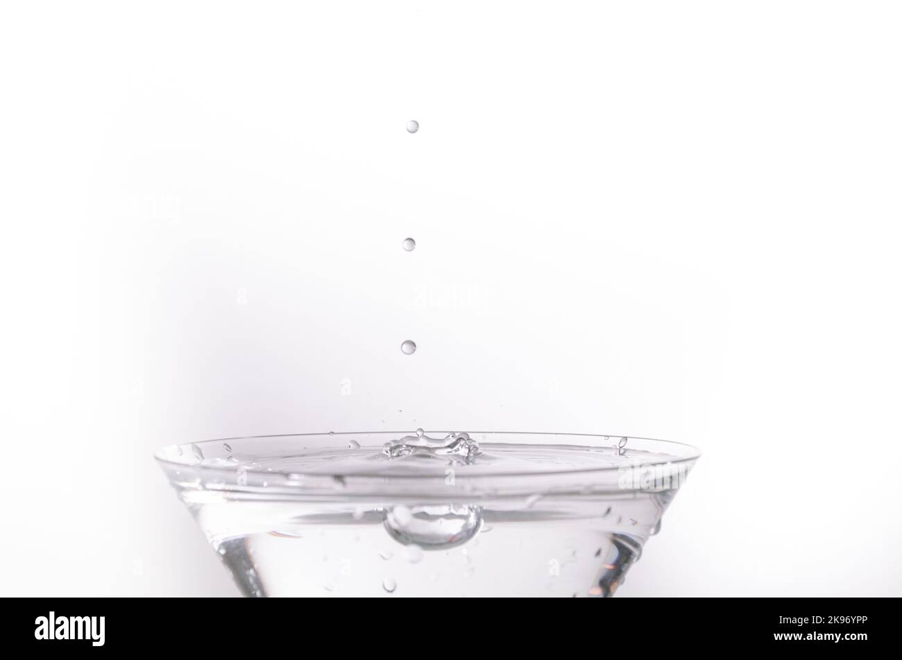 A close-up shot of a water drop falling into a glass on a white ...