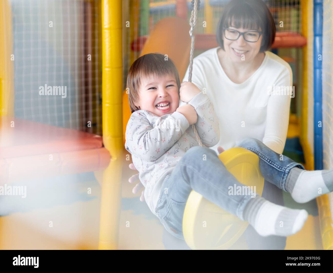 Toddler plays on rope swing with his mother or babysitter. Physical ...