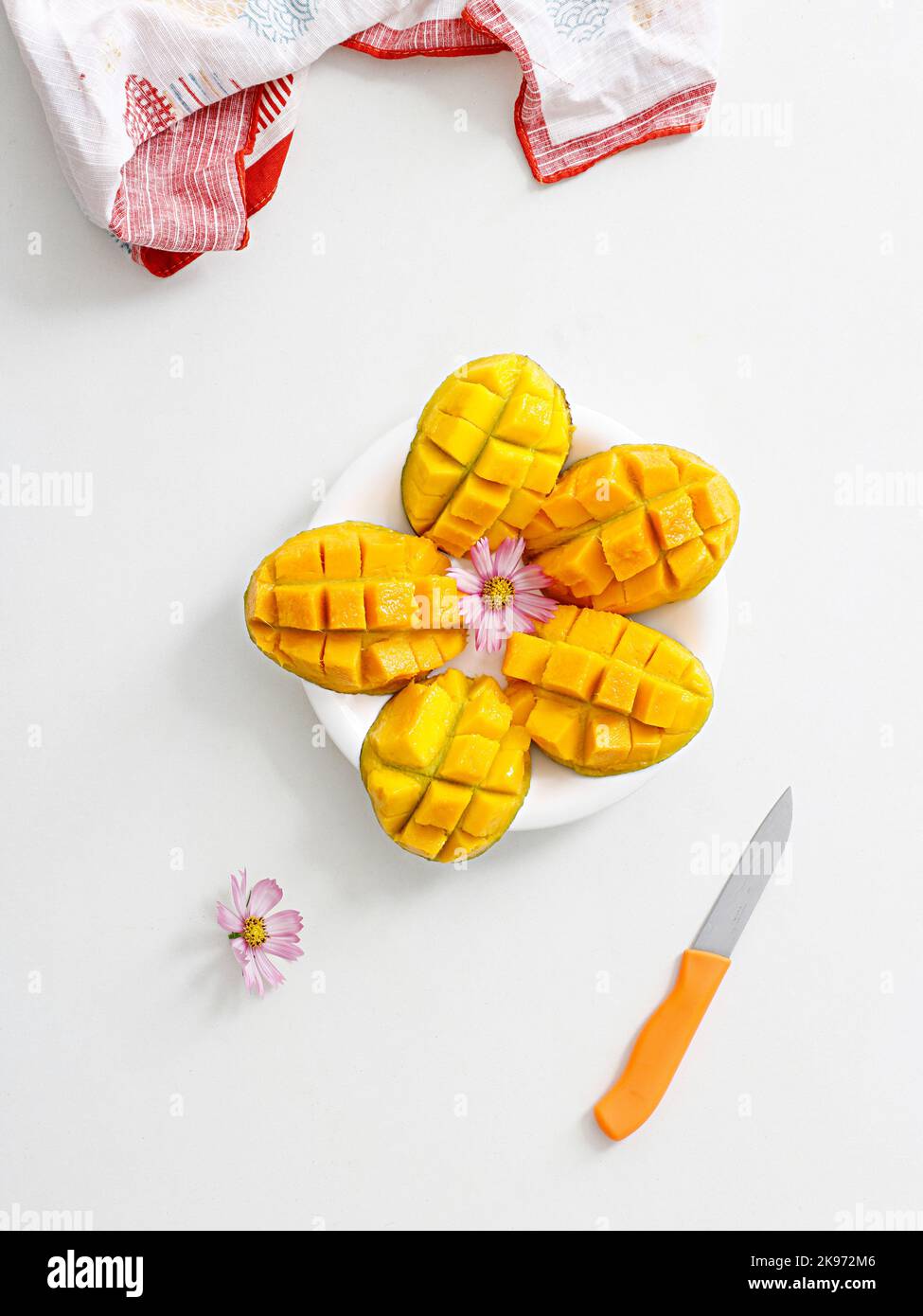 A flat lay of cut mangoes, a knife and pink flowers on a white ...