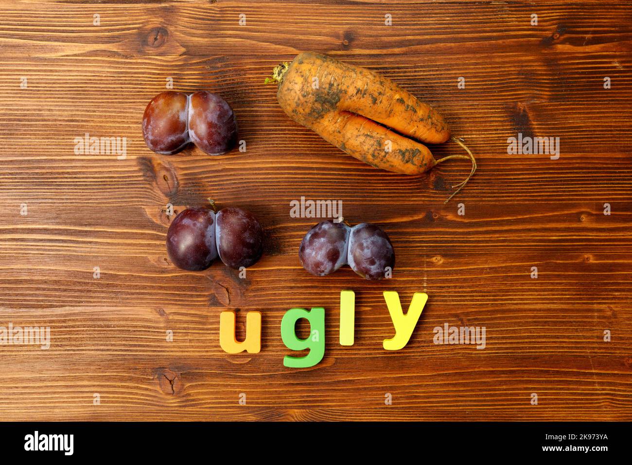 Ugly organic blue plums and carrot on wooden background. The ugly ...