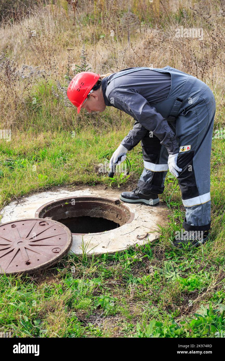 A male working plumber in overalls shines a flashlight into a water ...