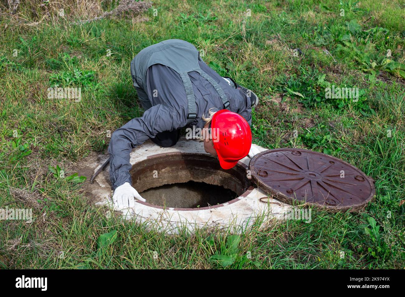 A male plumber opened the hatch of a water well and looks inside ...
