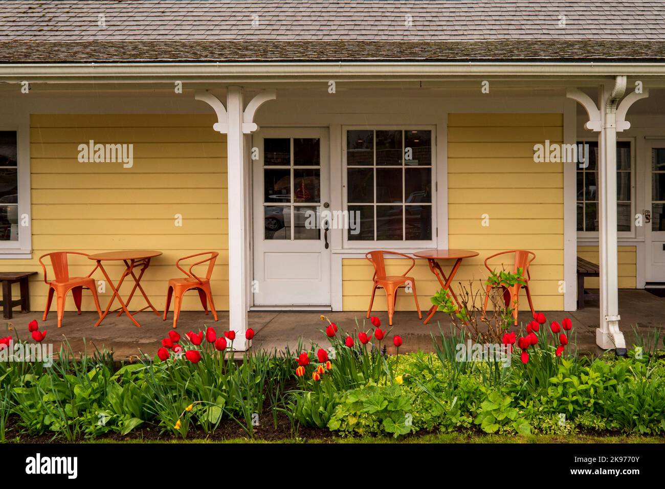 On a rainy day, orange cafe tables and chairs sit empty on the porch of ...