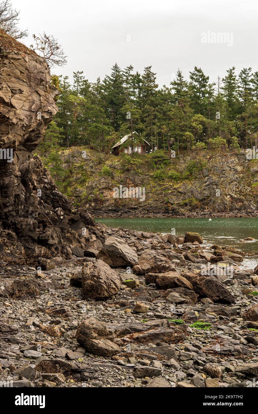 A log cabin sits perched on a cliff above a green bay on Orcas Island ...