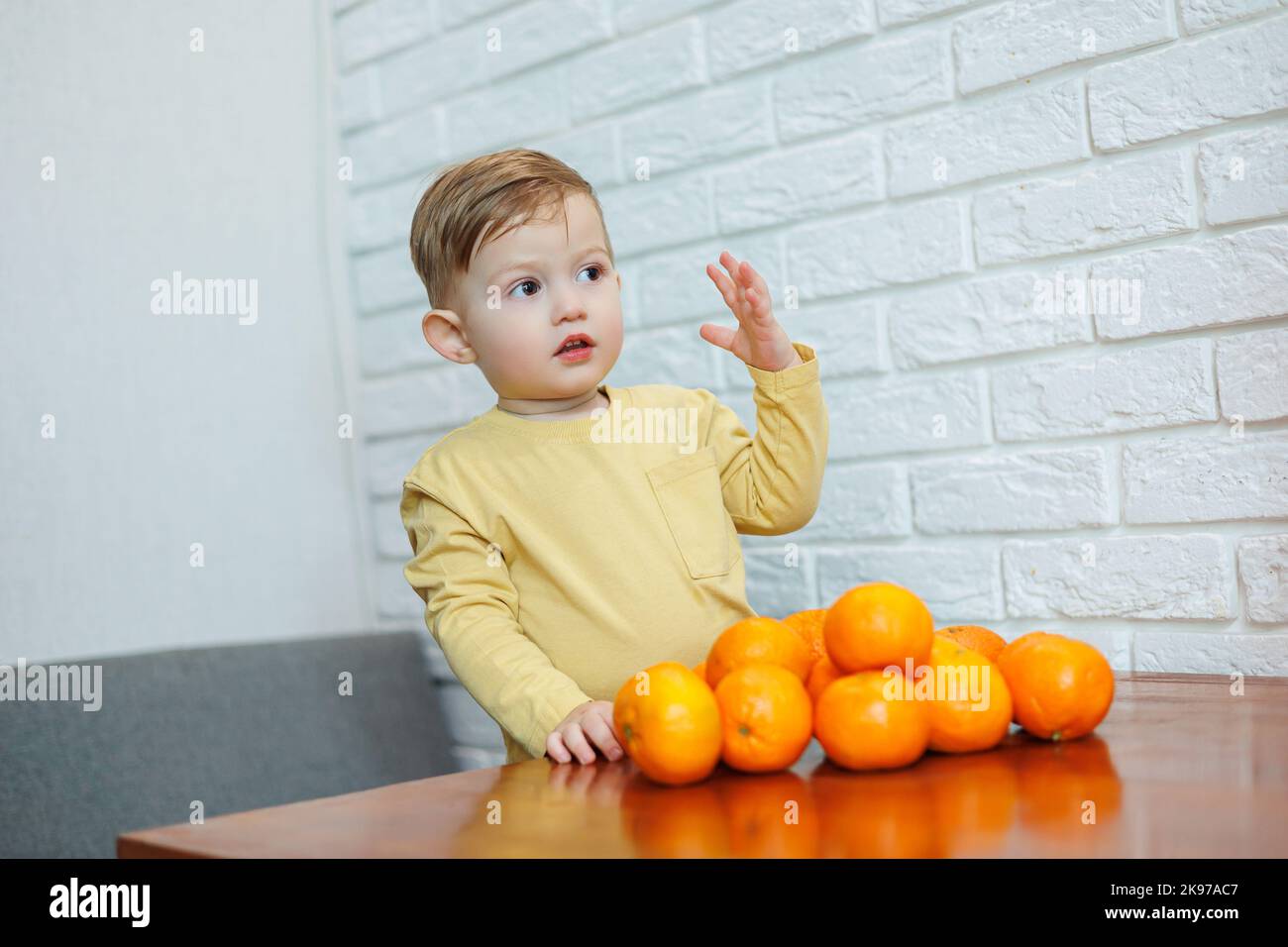 A little boy 2 years old holds tangerines in his hands. The kid wants ...