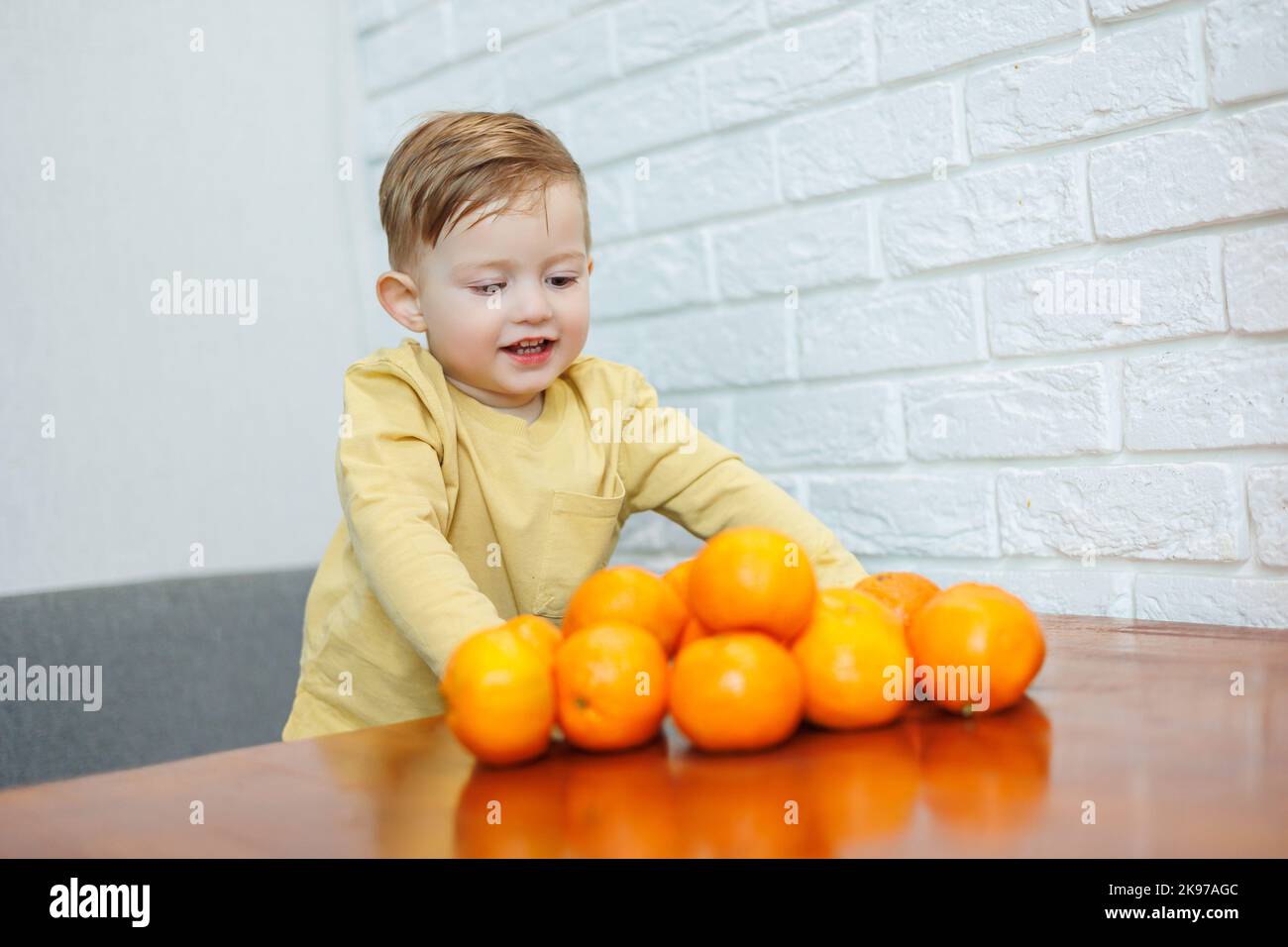 A little boy 2 years old holds tangerines in his hands. The kid wants ...