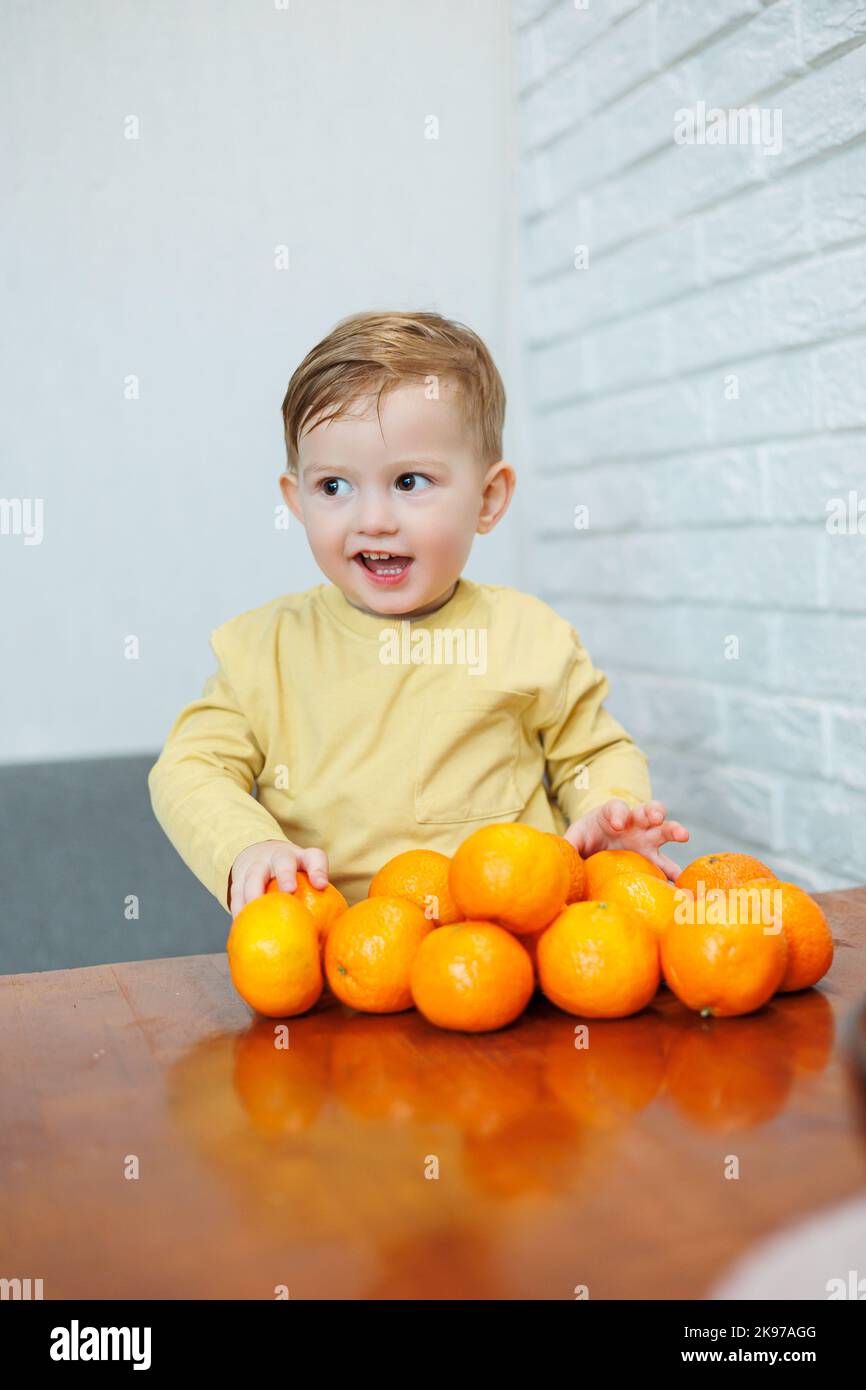 A little boy 2 years old holds tangerines in his hands. The kid wants ...