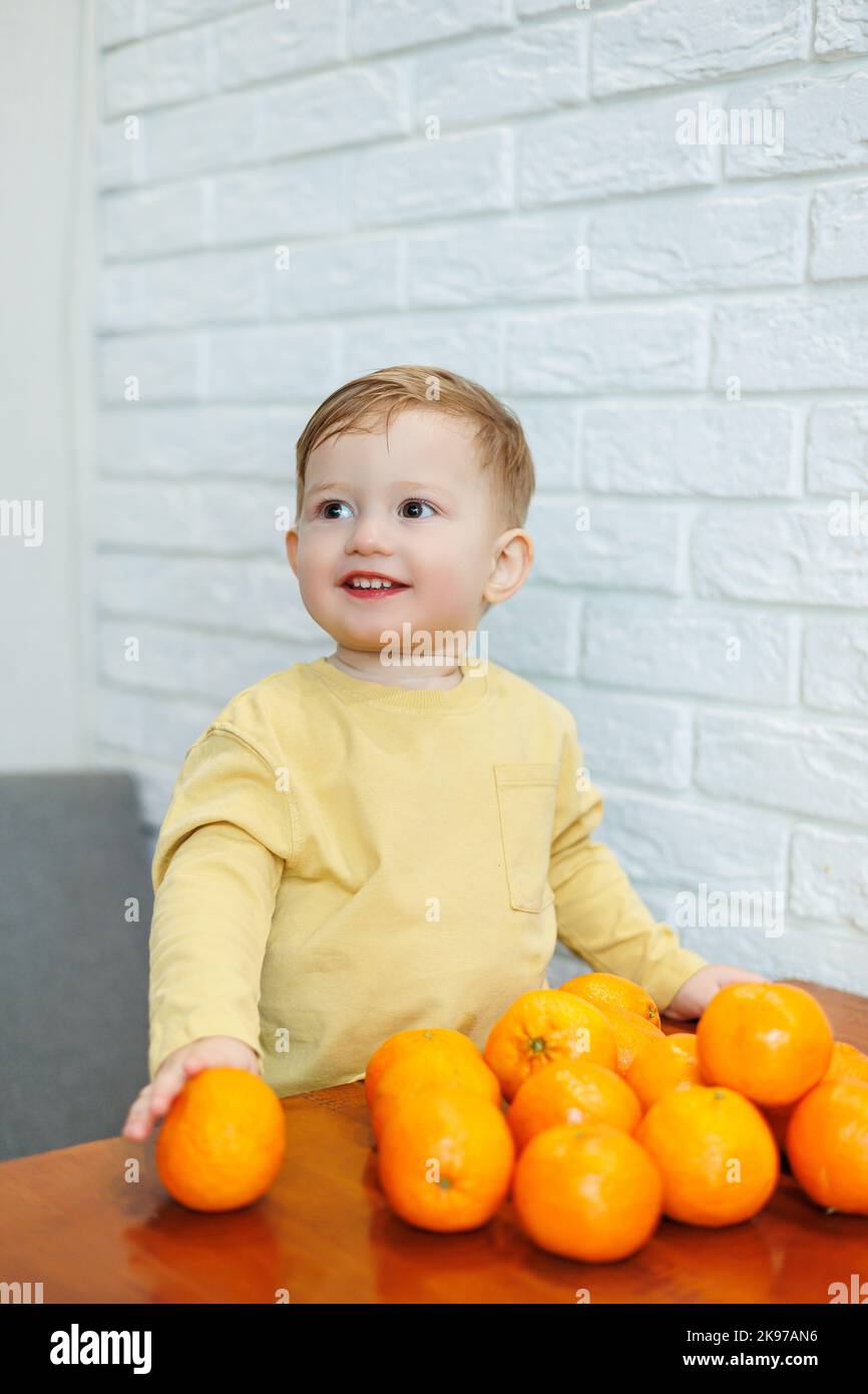 A little boy 2 years old holds tangerines in his hands. The kid wants ...