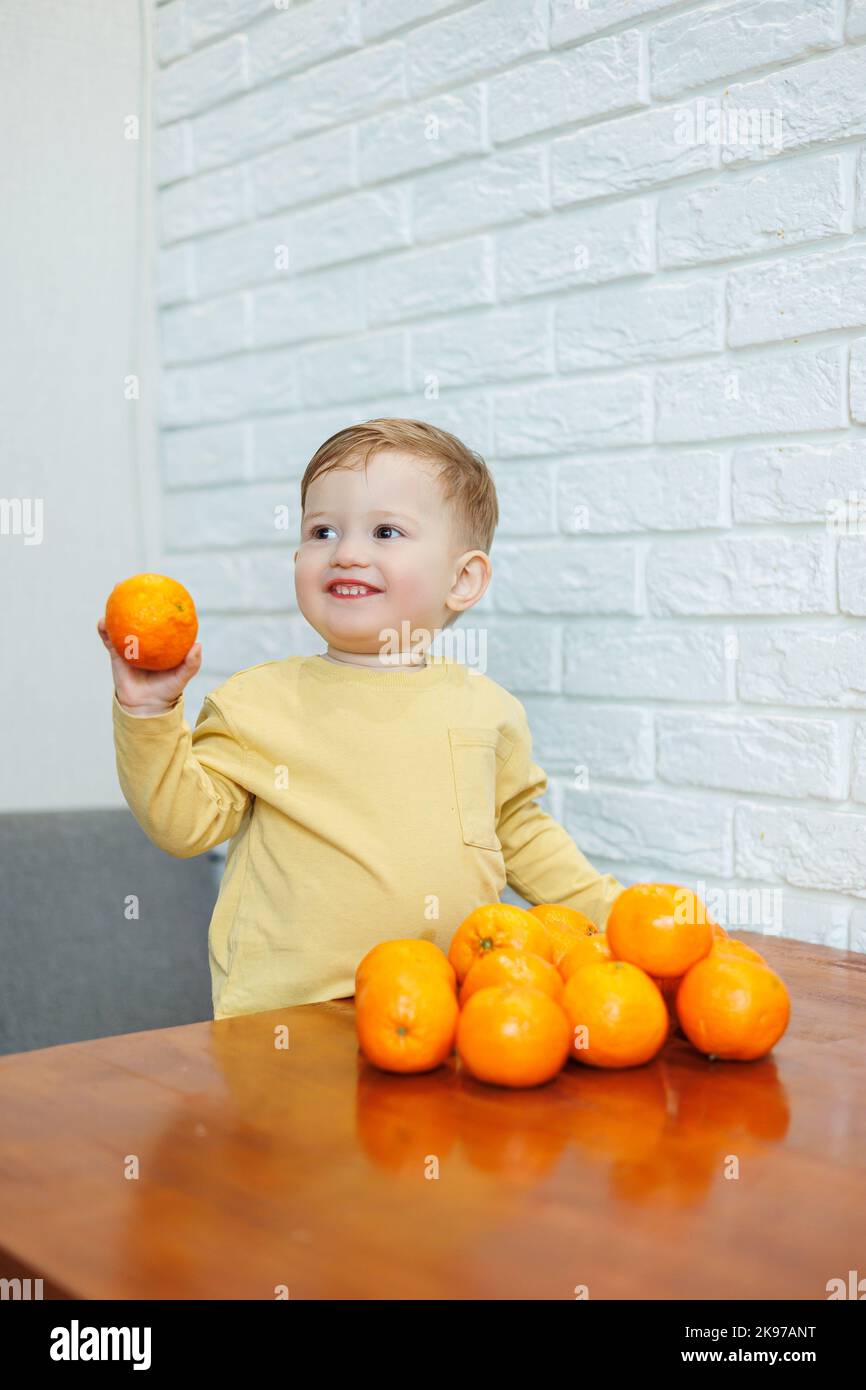 A little boy 2 years old holds tangerines in his hands. The kid wants ...