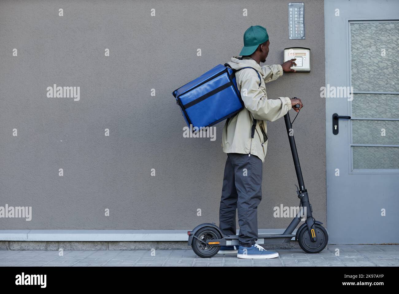 Food delivery worker ringing doorbell while riding electric scooter ...