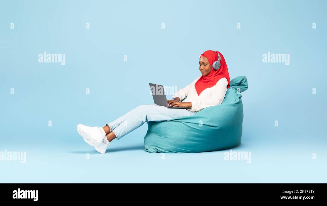 African american muslim woman using laptop and wearing headphones ...