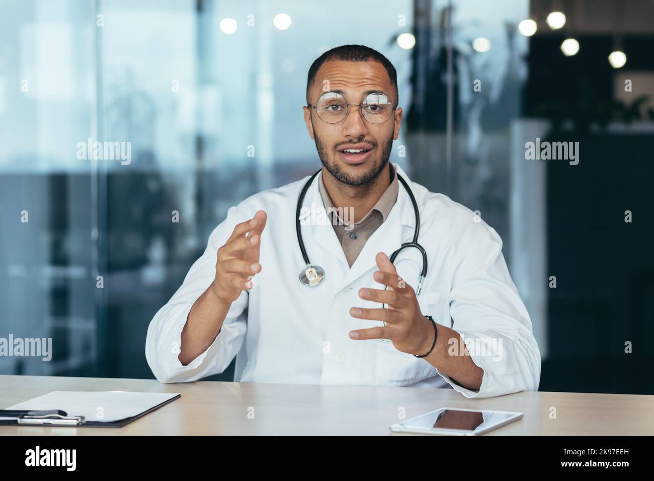 A young Latin American male doctor sits in the office facing the camera ...
