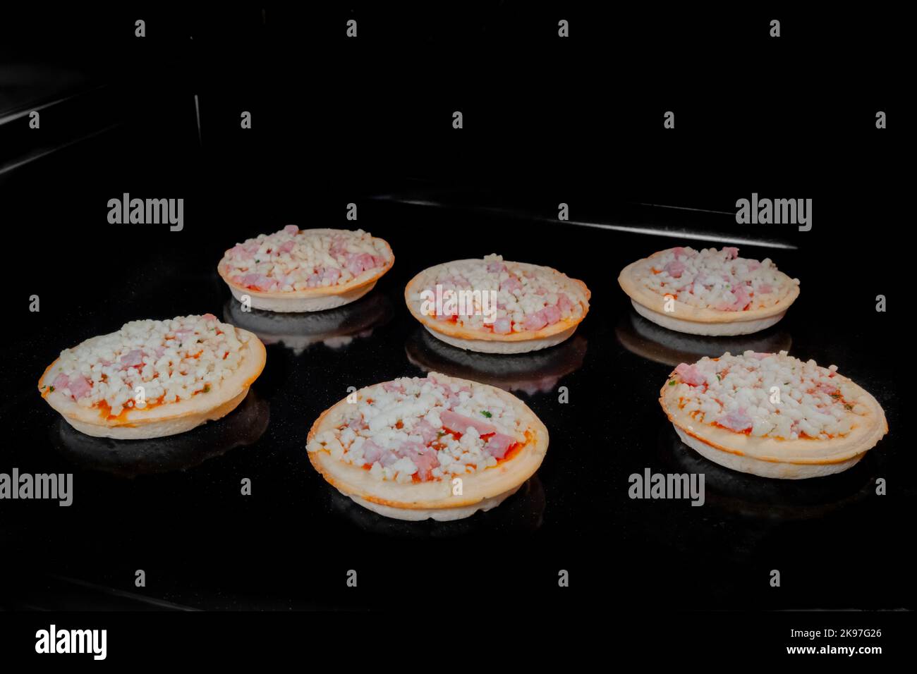 Six uncooked homemade mini pizzas on tray in electric oven, black background Stock Photo - Alamy