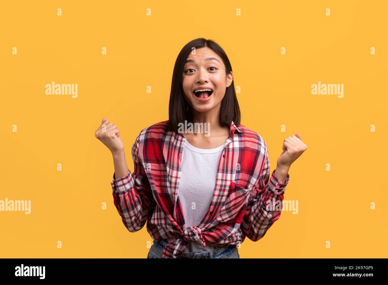 Triumphant asian lady shaking clenched fists and shouting in excitement ...