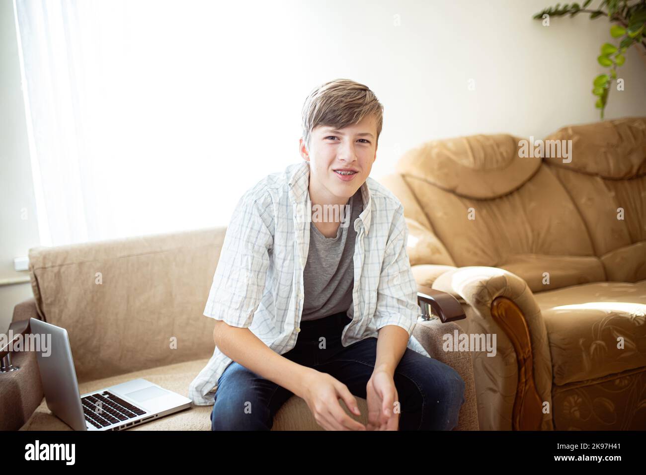 A teenager with braces on his teeth sits in the living room. The ...