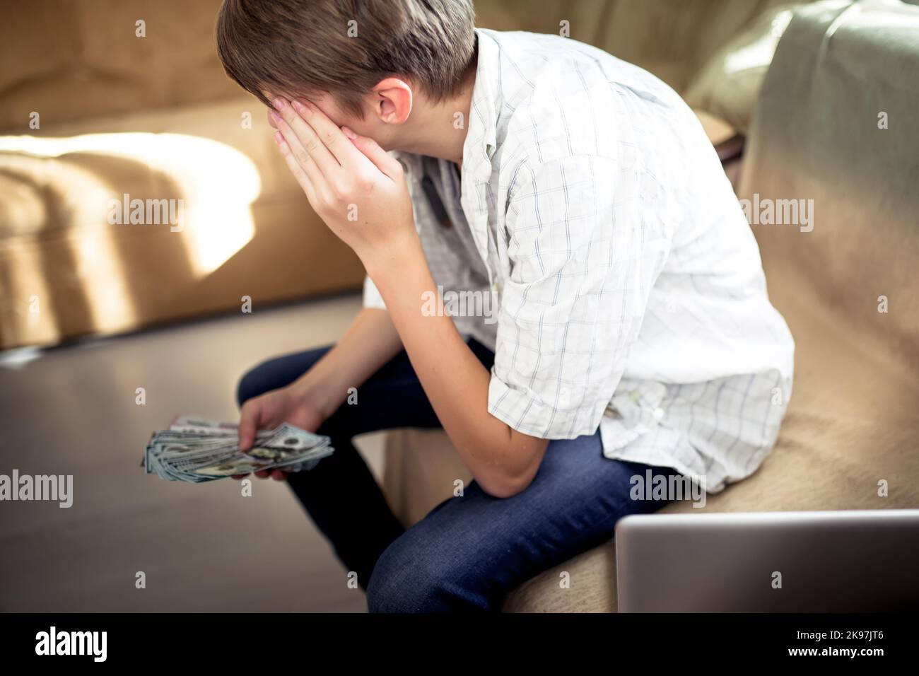 boy is holding on to head. A sad teenager with a wad of dollars in ...